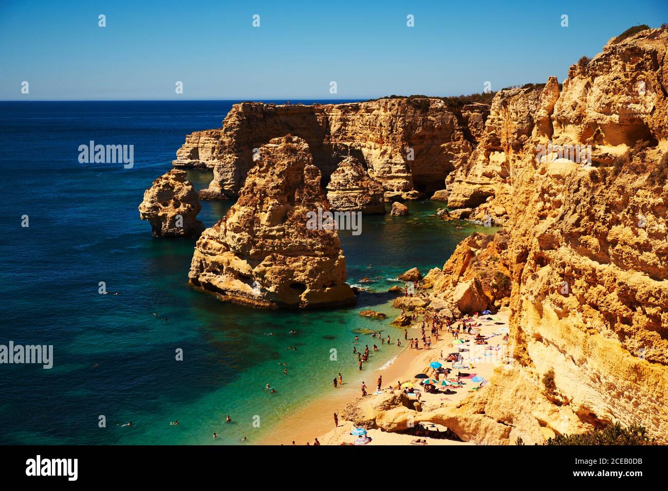 Sunny beach with many people and umbrellas with big tall rocks and ...