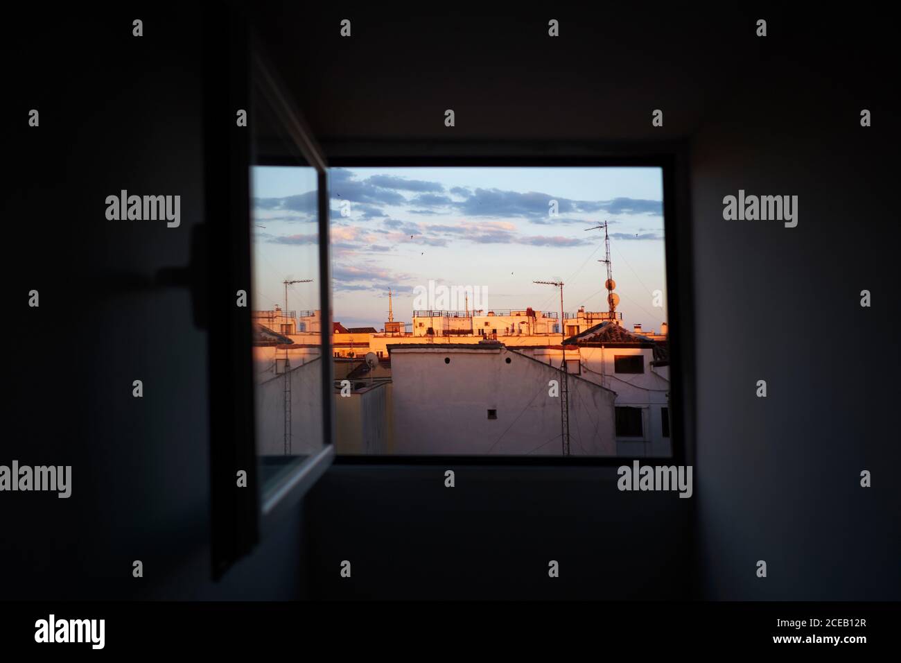 Rooftops of houses with antennas under blue cloudy sky through opened ...