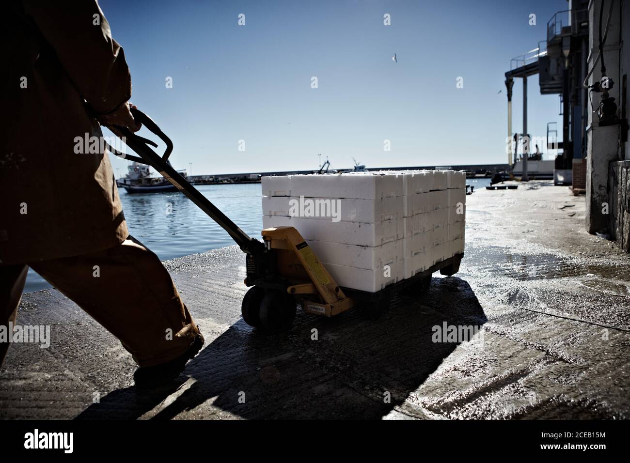 Crop side view of man in uniform pulling cart loaded with white boxes ...