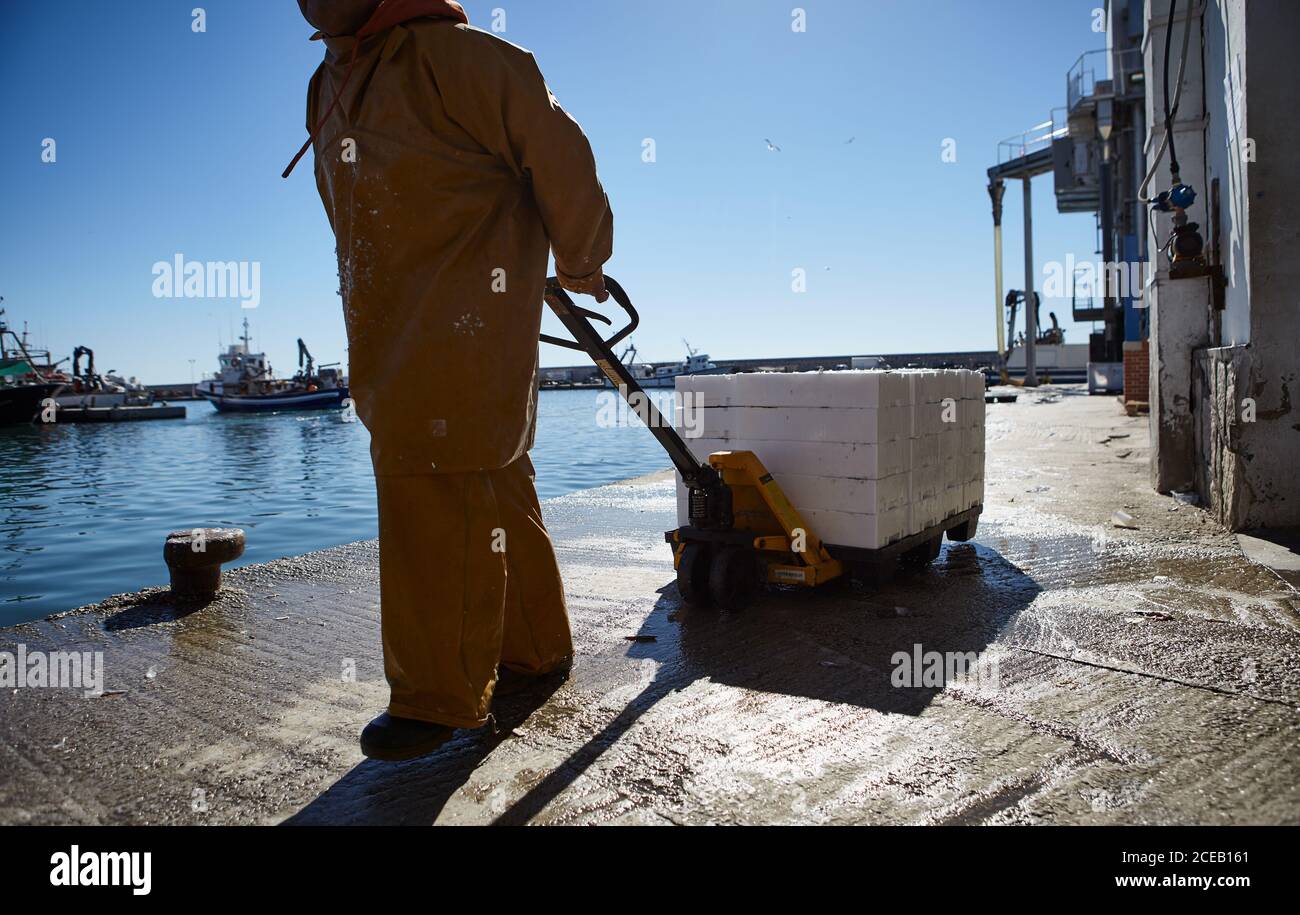 Crop side view of man in uniform pulling cart loaded with white boxes ...
