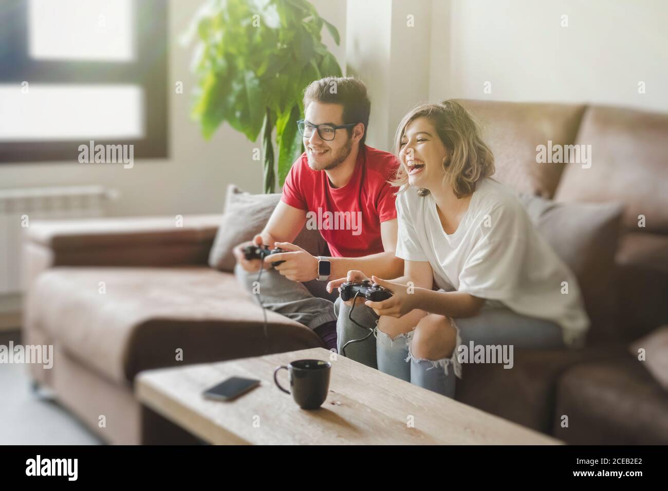 Young couple sitting on couch with gamepads and playing on console at ...
