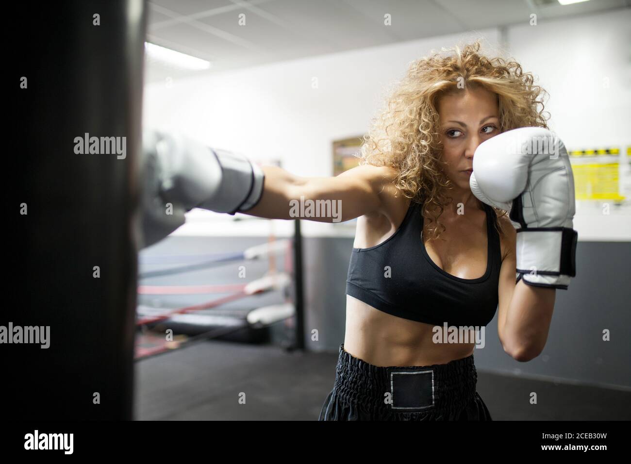 Adult fitness lady with curly hair in boxing gloves fighting on ring in ...
