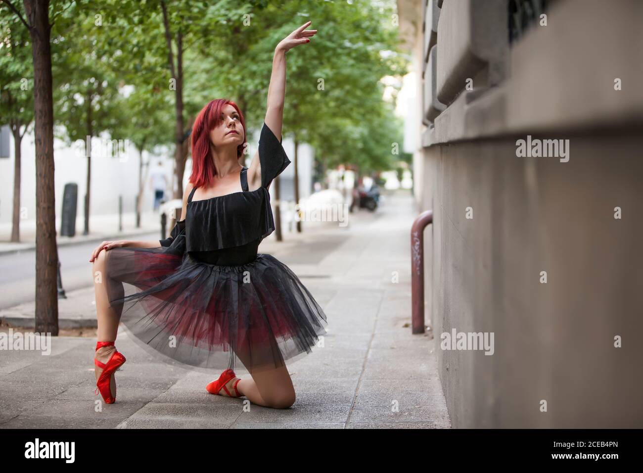 Red head ballerina with black tutu and red ballet tips warming up to ...