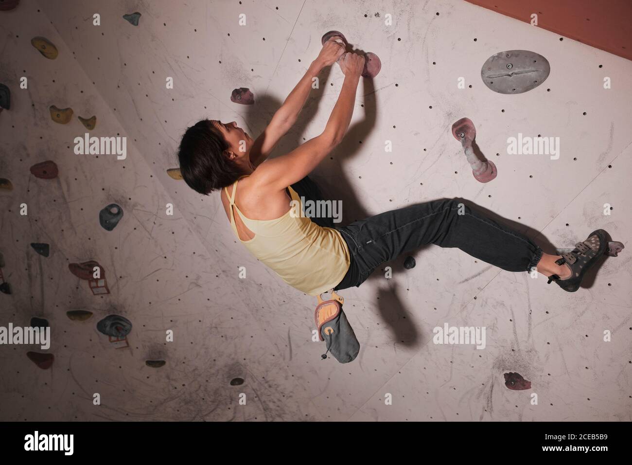 Back view of young lady in sportswear training on climbing wall with ...