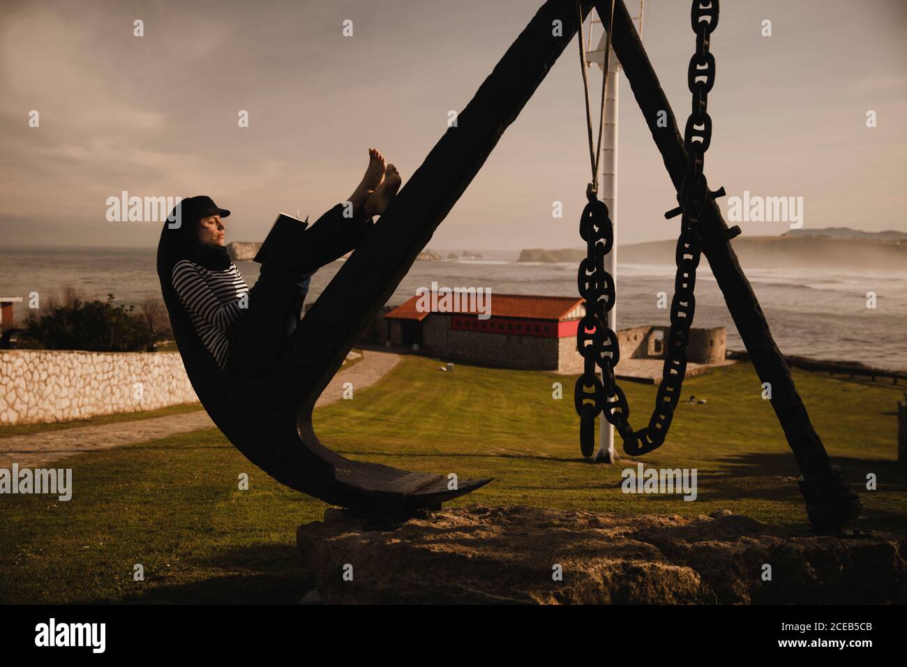 Side view of elegant lady in cap reading volume and sitting on abstract ...