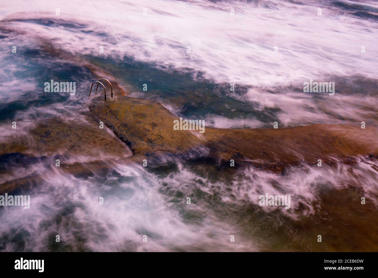 From above rock coast with ladder between water surface with foam in ...