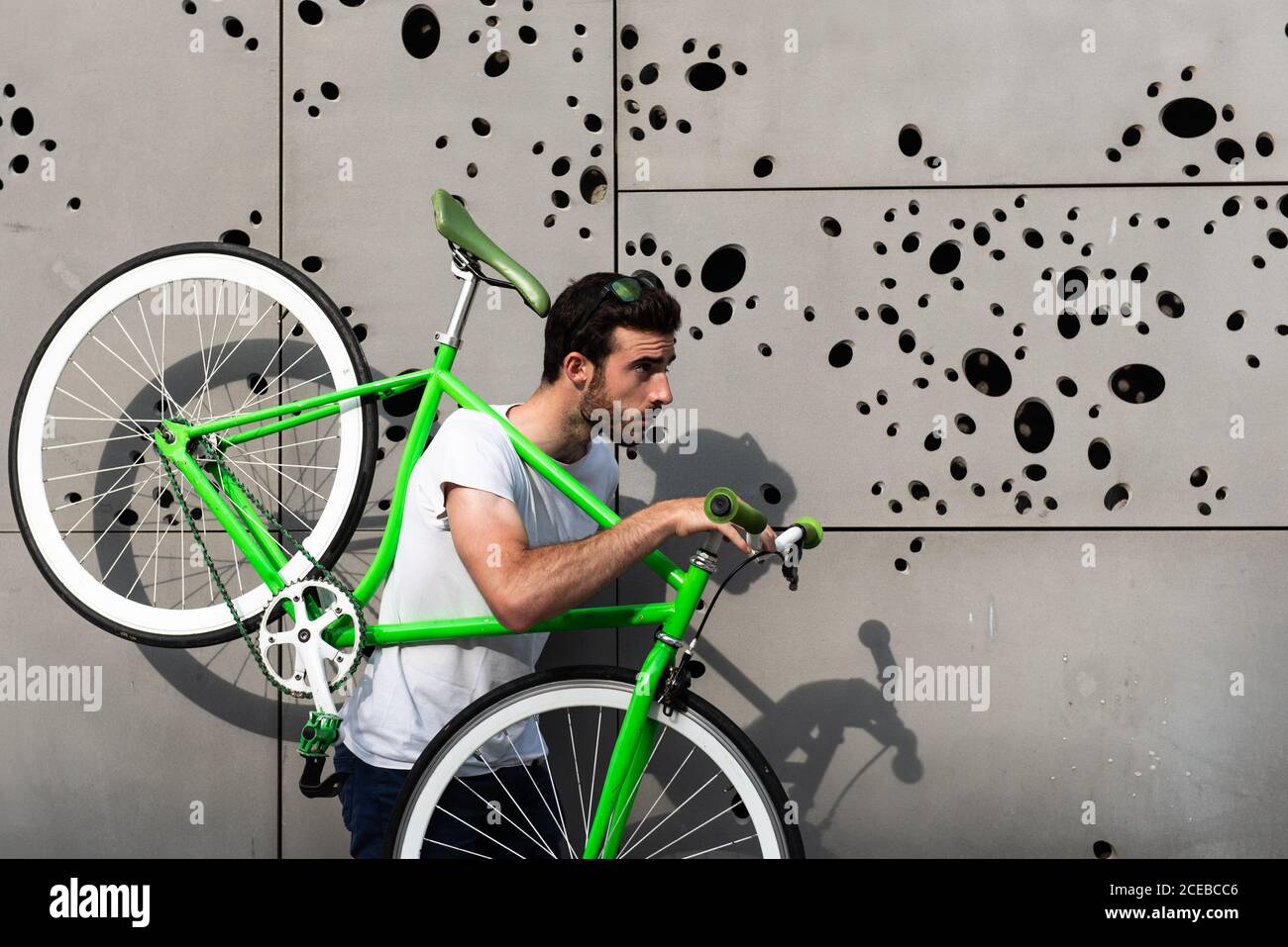 Side view of young man carrying green cycle in the city Stock Photo - Alamy