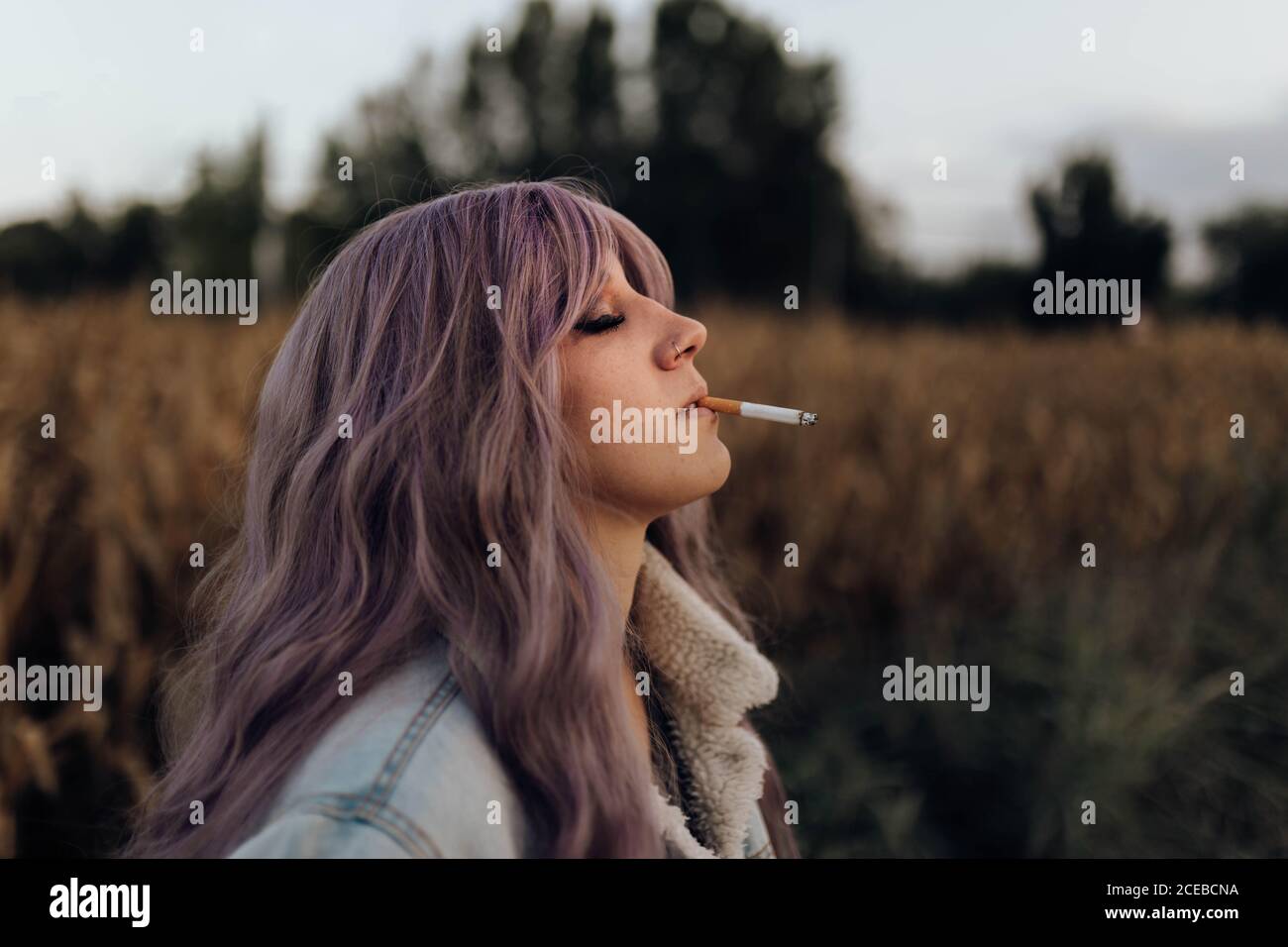 Side view of beautiful modern Woman with pink hair smoking cigarette ...