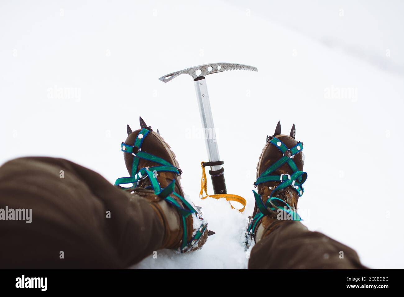 Legs of unrecognizable climber and pickaxe on hill covered with snow ...