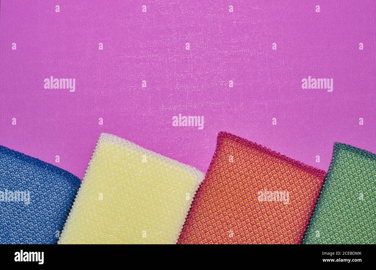 Colorful cleaning sponges lined up on a textured peony color background ...