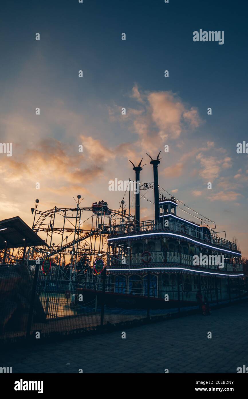 Roller coaster and tourist†boat near amusement park and embankment with ...
