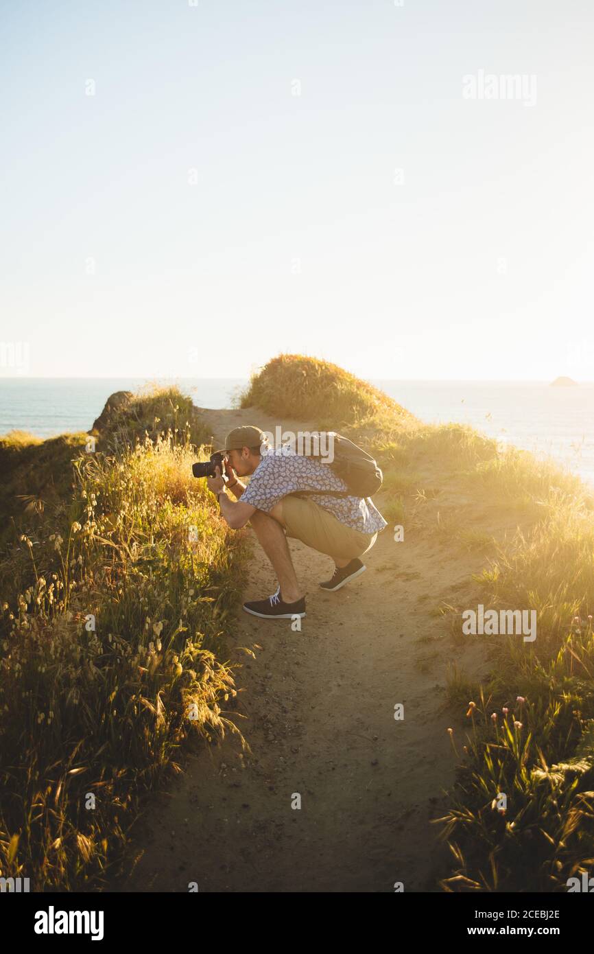 Side view of young guy using professional photo camera to take photos ...