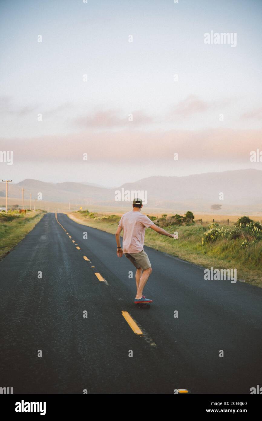 Side view of young man in casual outfit riding skateboard along asphalt ...
