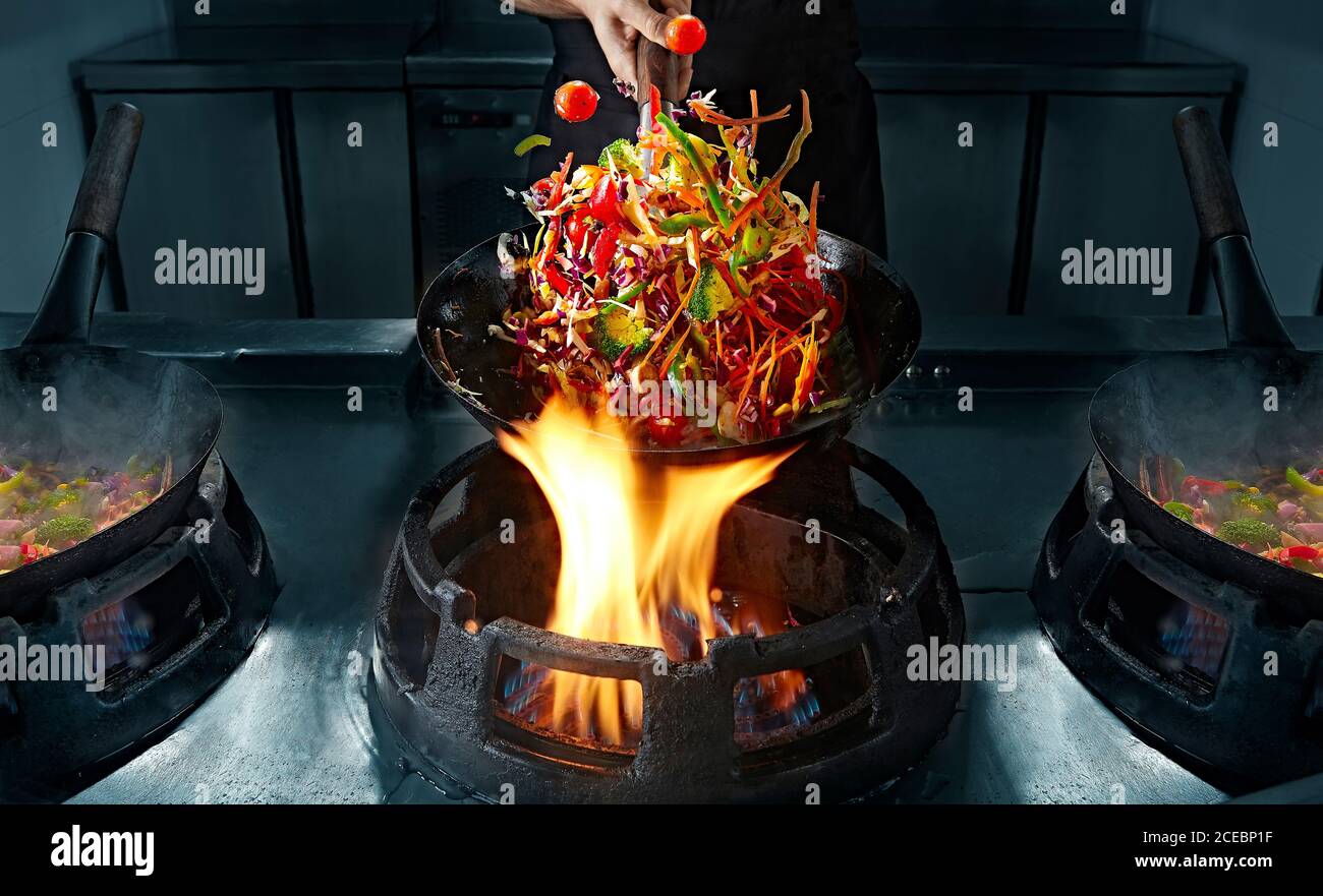 crop hand cooking wok on pan over fire and moving vegetables in the air ...
