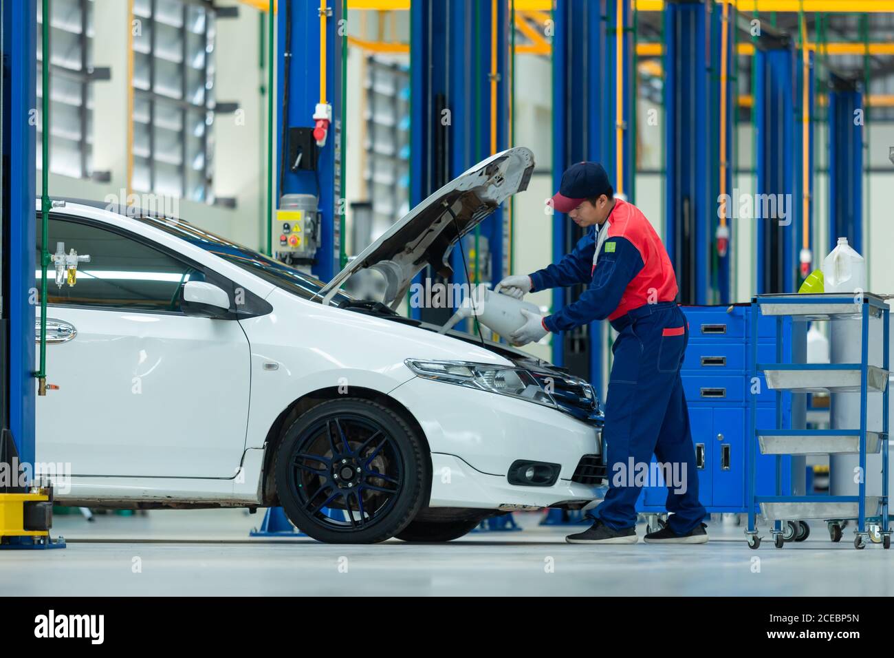 Asian servicing mechanic pouring new oil lubricant into the car engine ...