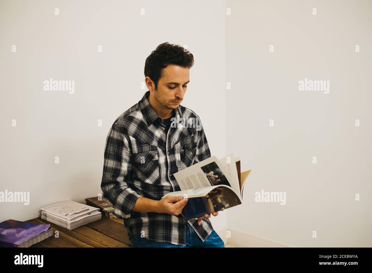 Young man holding magazine near table in room Stock Photo - Alamy