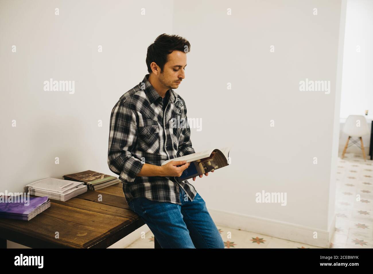 Young man holding magazine near table in room Stock Photo - Alamy