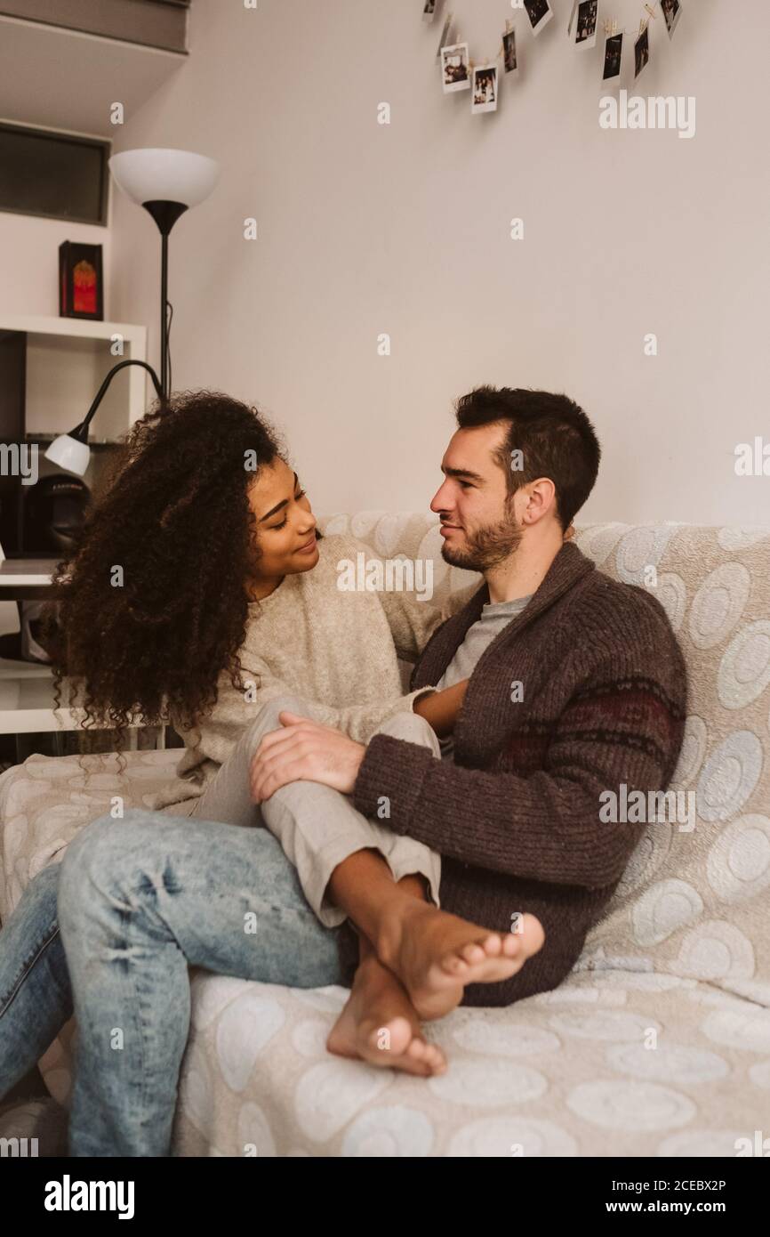 Young multiracial couple hugging on sofa Stock Photo - Alamy