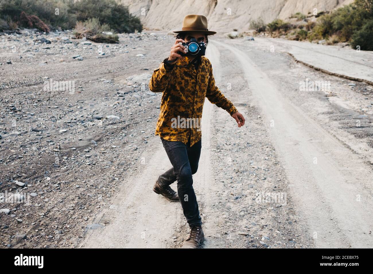 Adult modern man in colorful shirt and hat taking photo with camera ...
