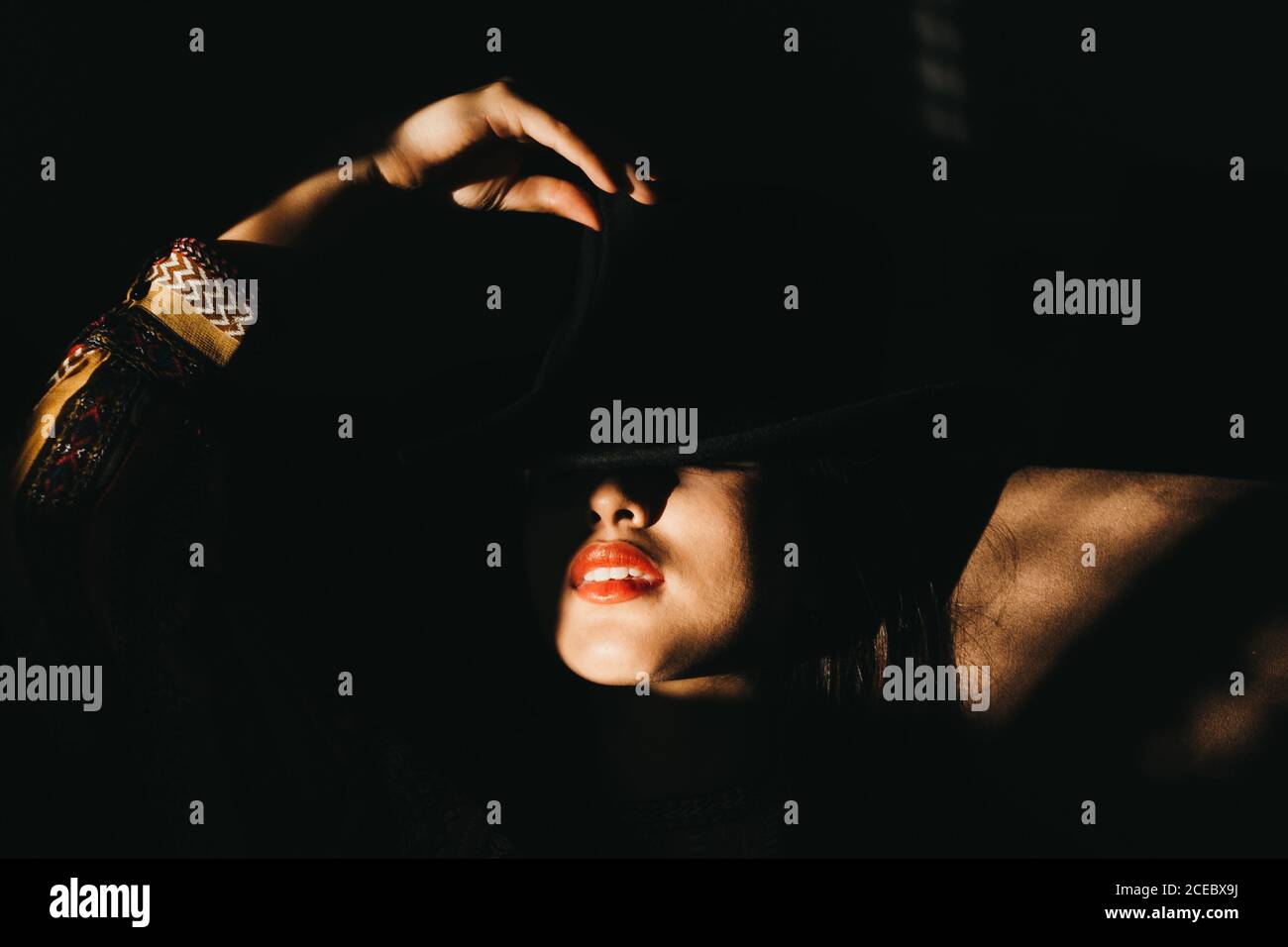 Attractive young female covering half of face with hat while standing ...