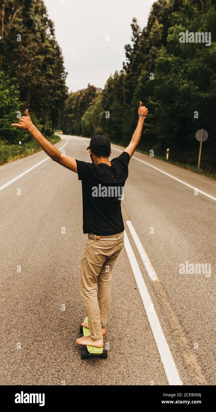 Back view of young barefoot man showing shaka sign and riding ...