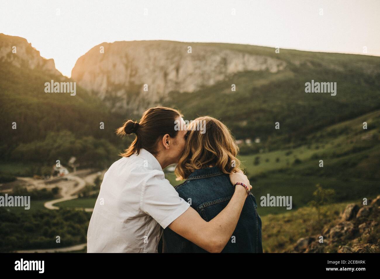Cute couple hugging and toughing foreheads while sitting on rocky slope ...