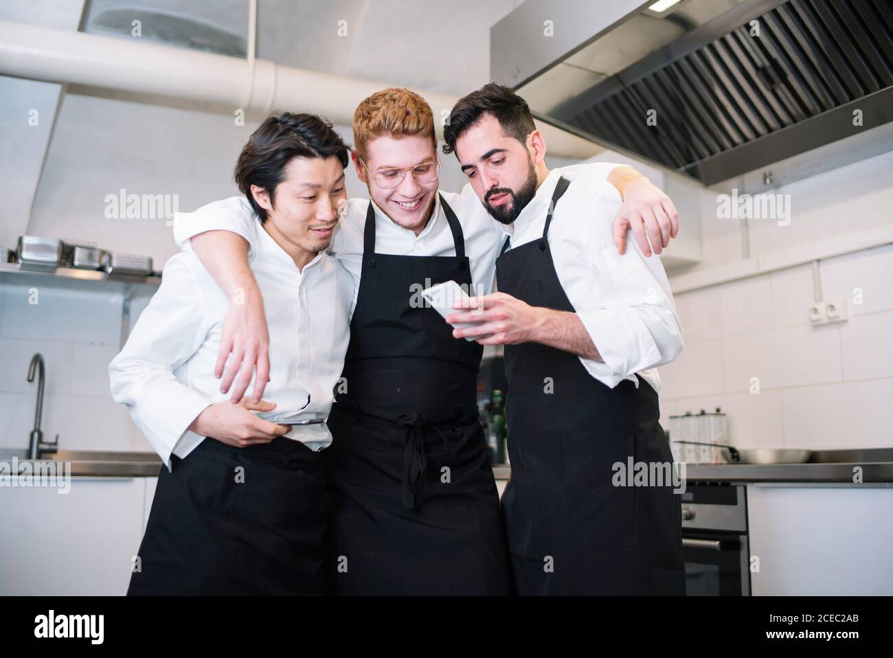 Three diverse men in cook uniform laughing and browsing smartphones ...