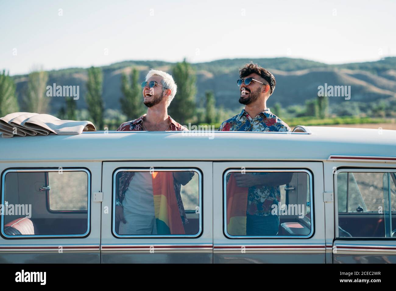 Two young men hugging and holding waving LGBT flag over heads while ...