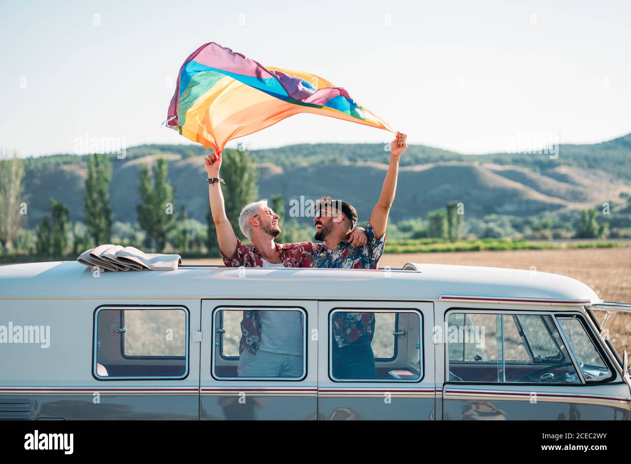 Two young men hugging and holding waving LGBT flag over heads while ...