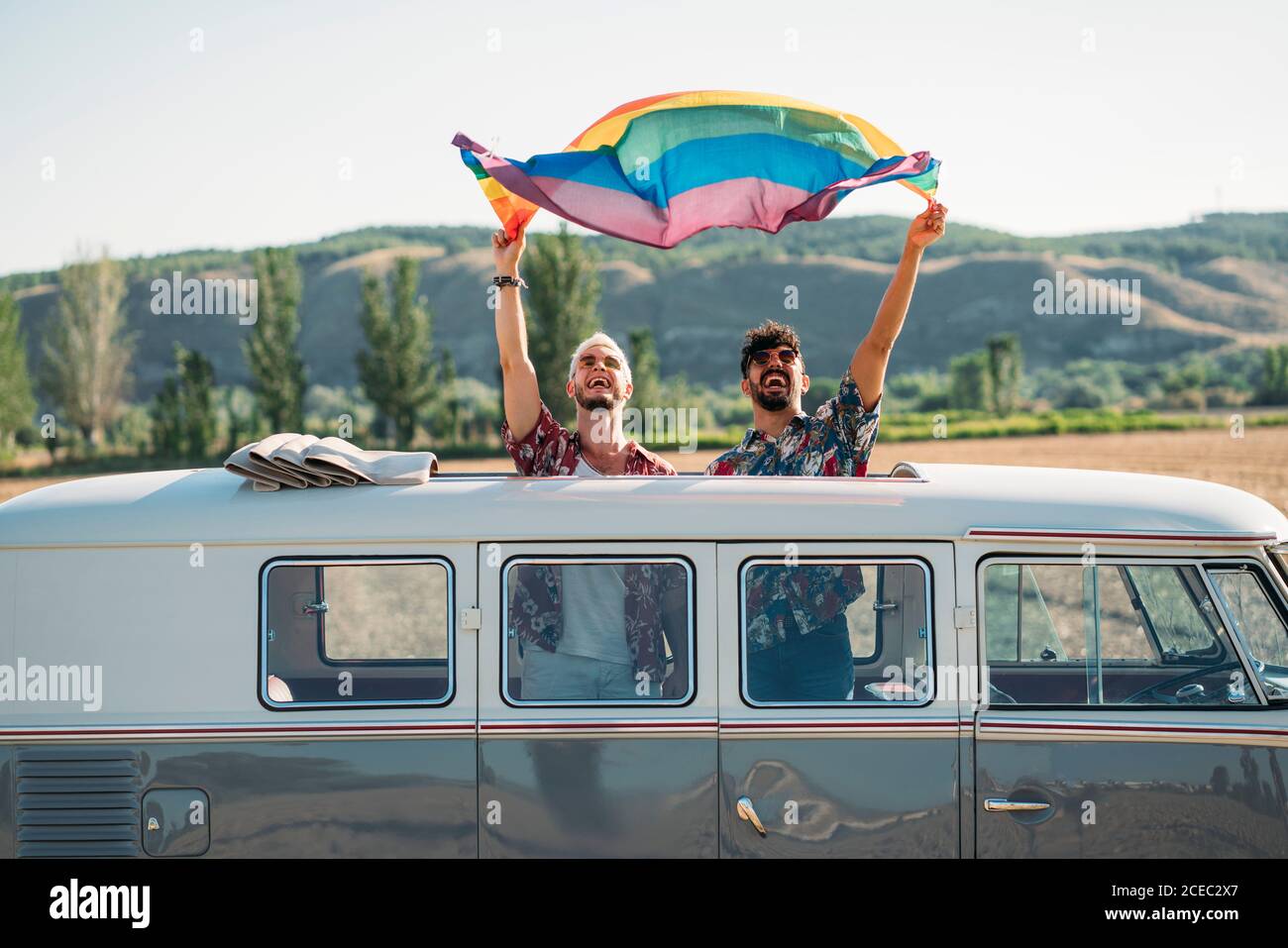 Two young men hugging and holding waving LGBT flag over heads while ...