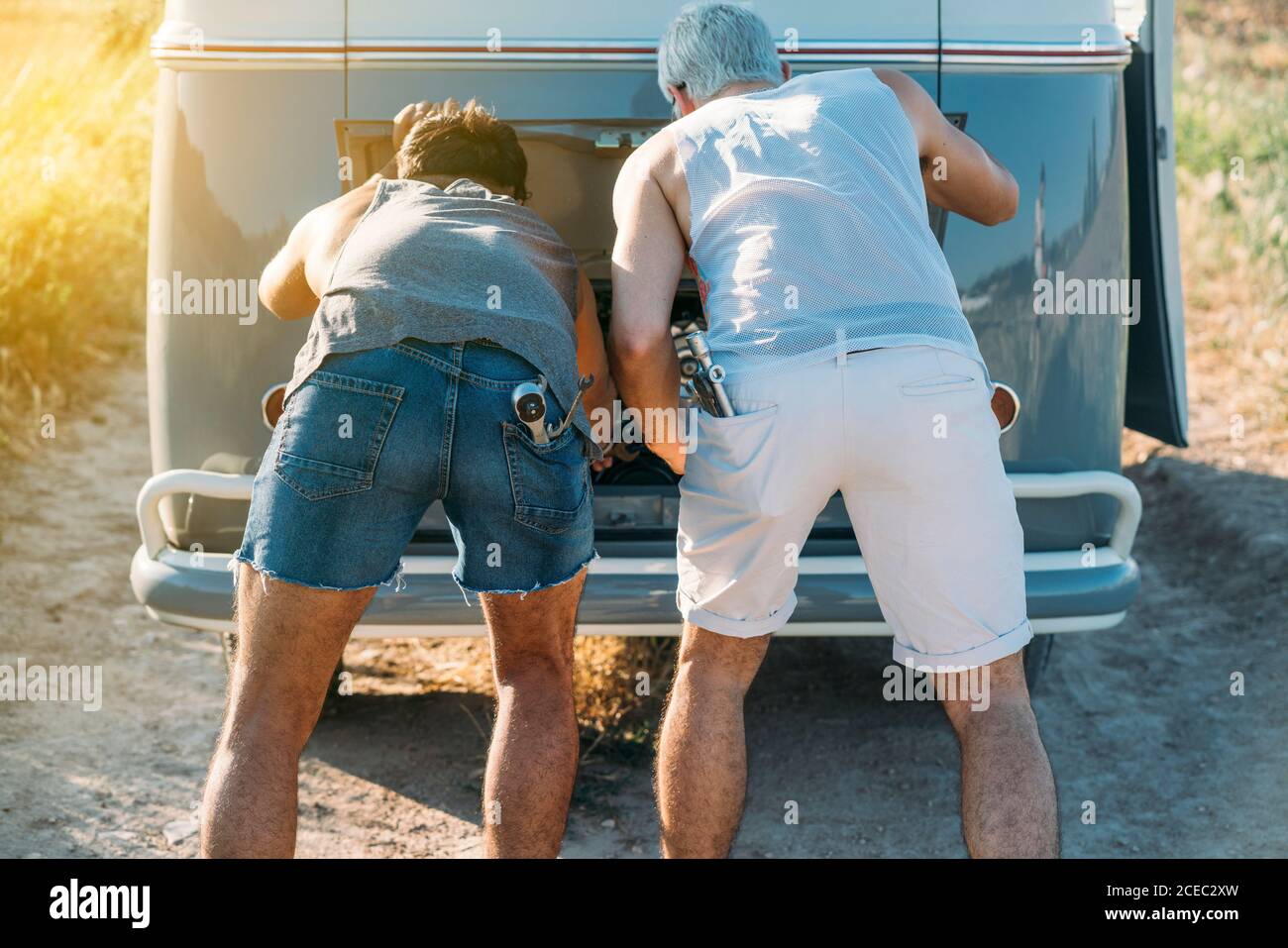 Back view of two guys fixing motor of retro van while traveling in ...