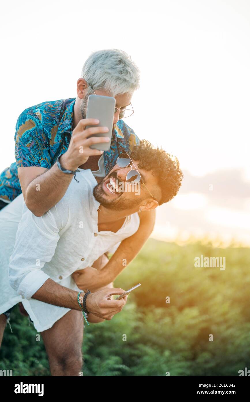 Handsome bearded guy giving piggyback ride to cheerful boyfriend and ...