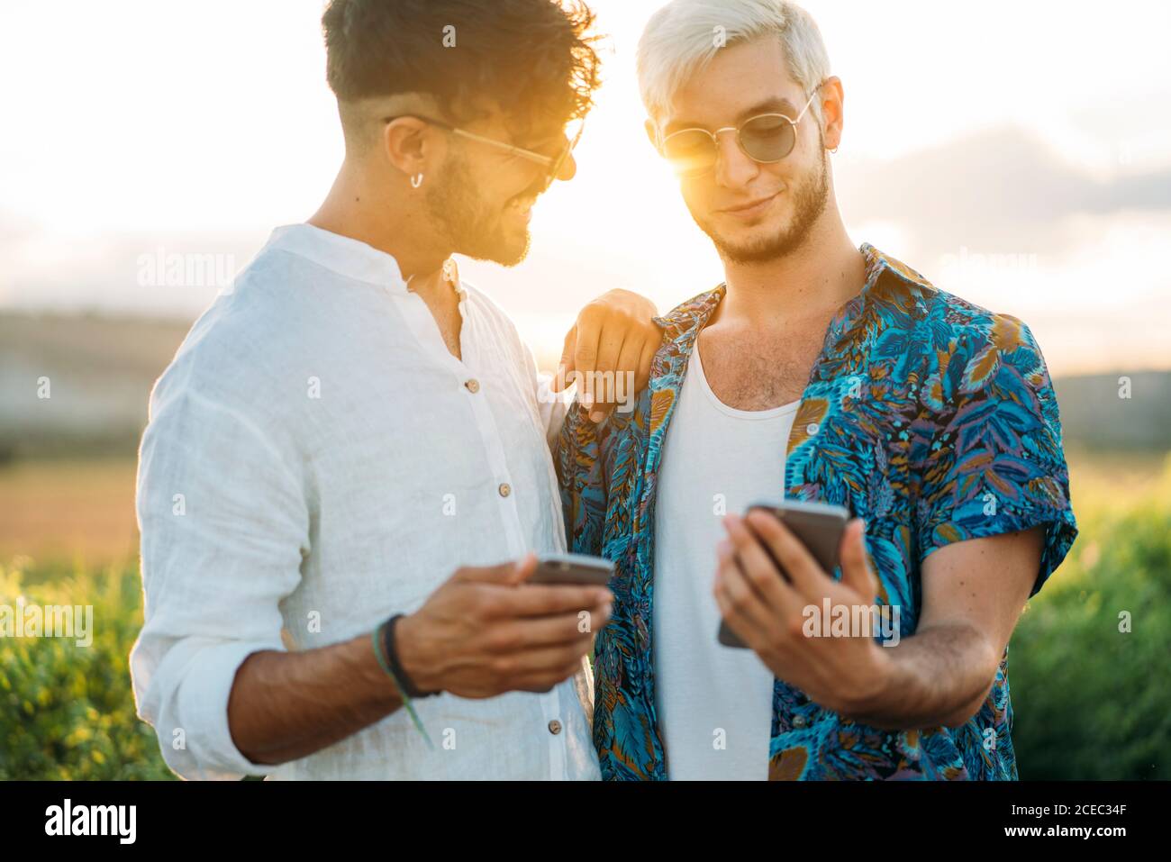 Two smiling men hugging and browsing smartphones while standing in ...