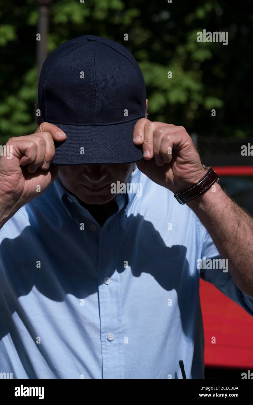 anonymous man in blue shirt wearing cap covering face while standing ...