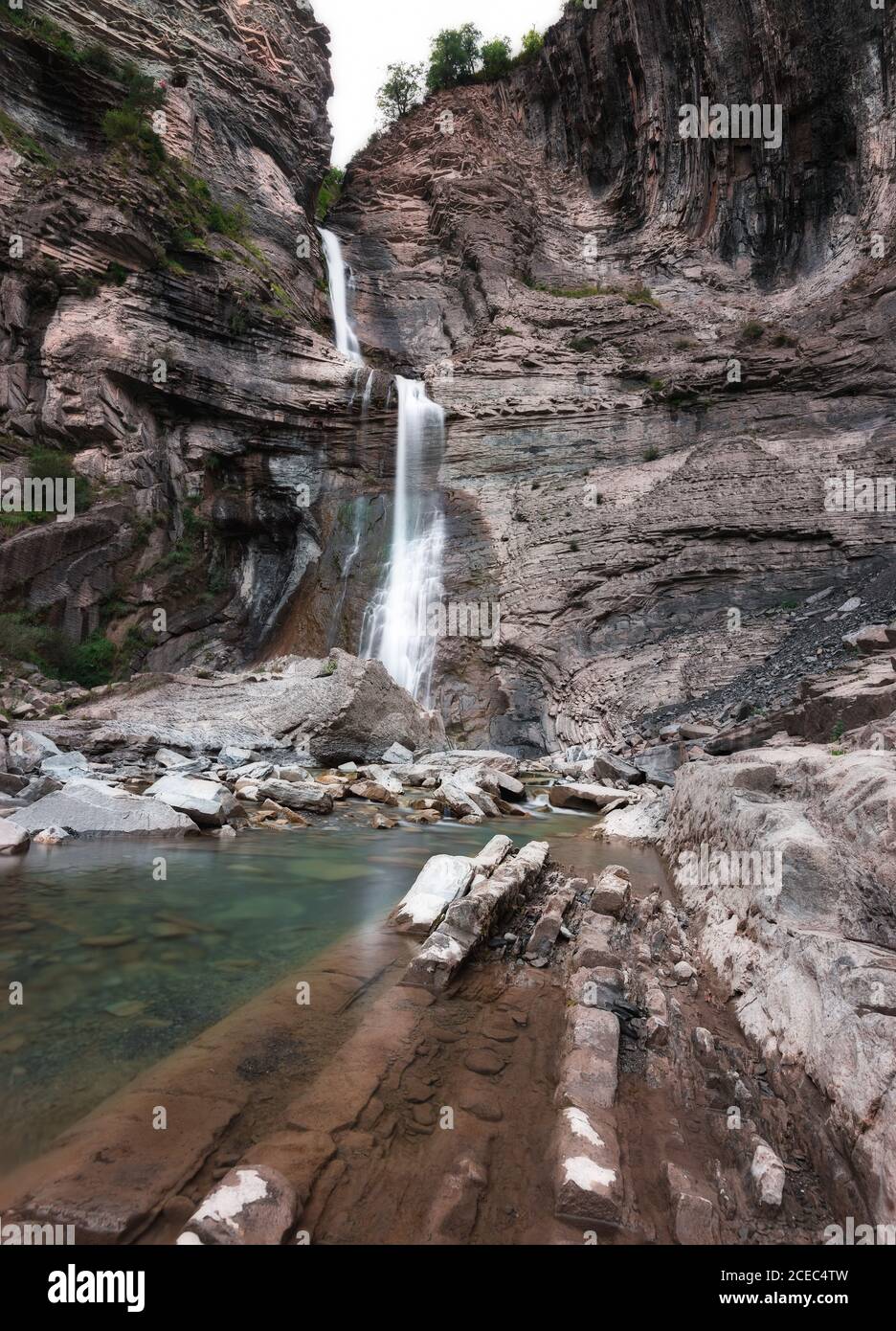 High steep cliff with little cascade waterfall flowing into pure river ...
