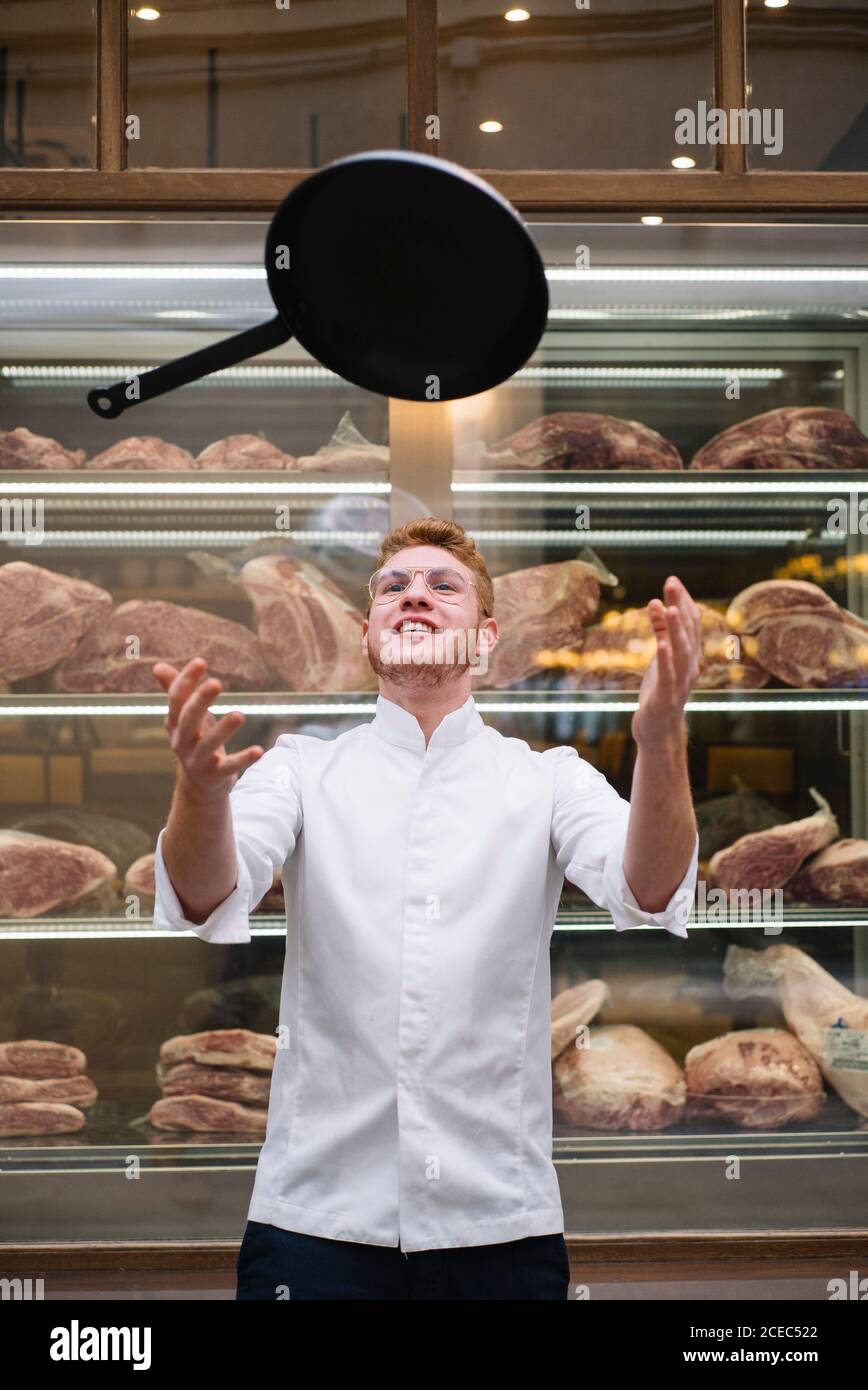 Chef cook in glasses and white gown throwing up frying pan working in ...
