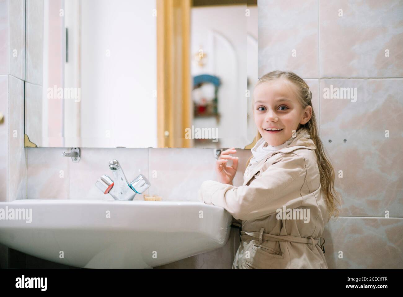 Side view of cheerful young girl standing at sink in coat and looking ...