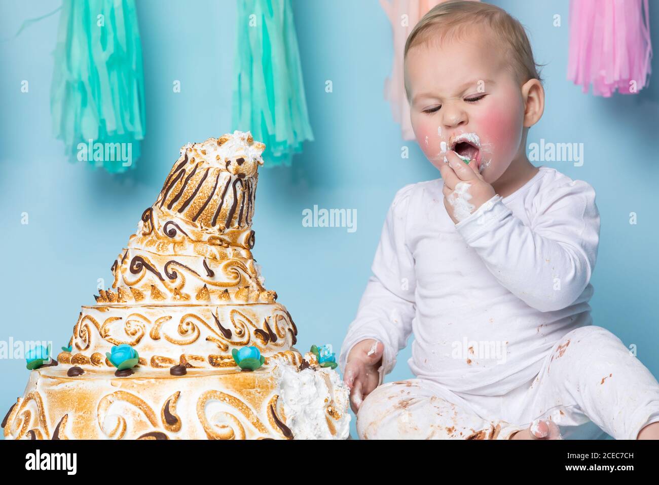 Cute little boy sitting at birthday cake and eating it with hand on ...