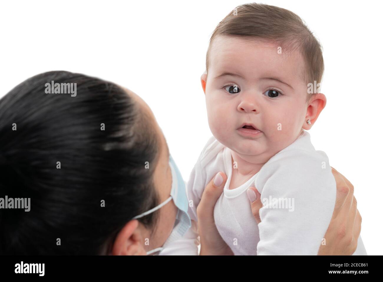 Close-up of baby girl held by adult mother wearing medical mask as ...