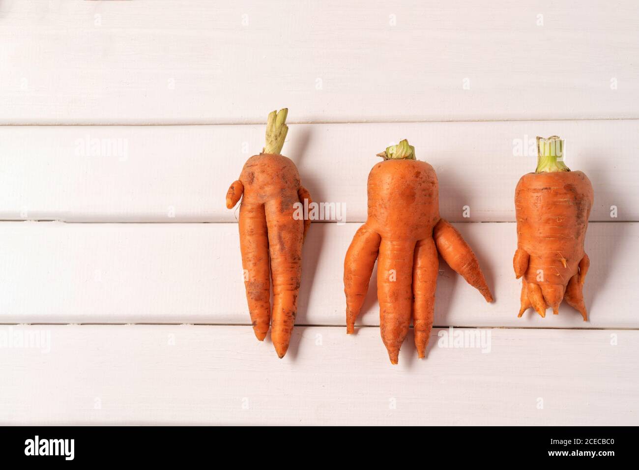 Ugly curved carrots on a white wooden background Stock Photo - Alamy
