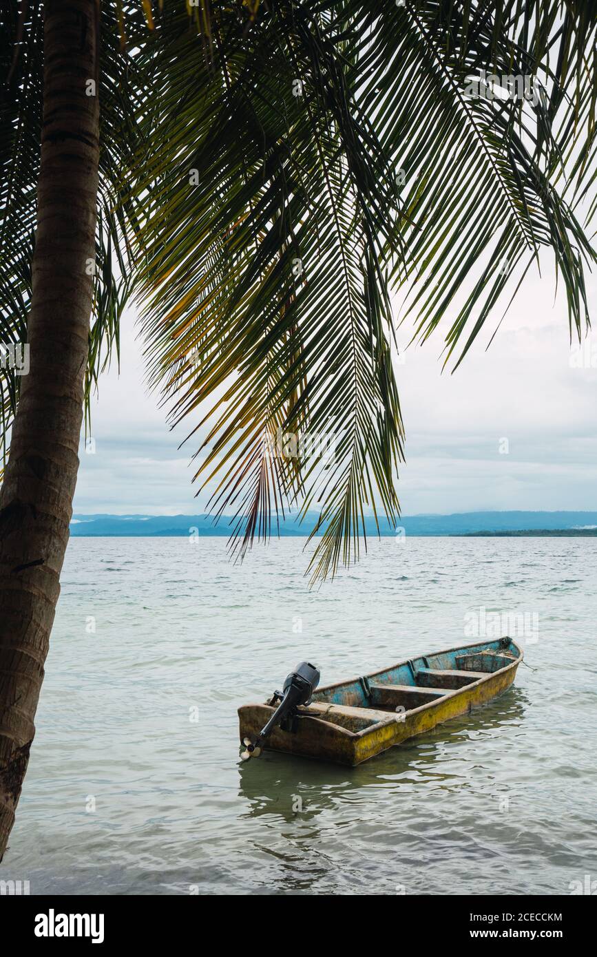 Empty aged boat with motor floating on sea water near palm in Panama ...