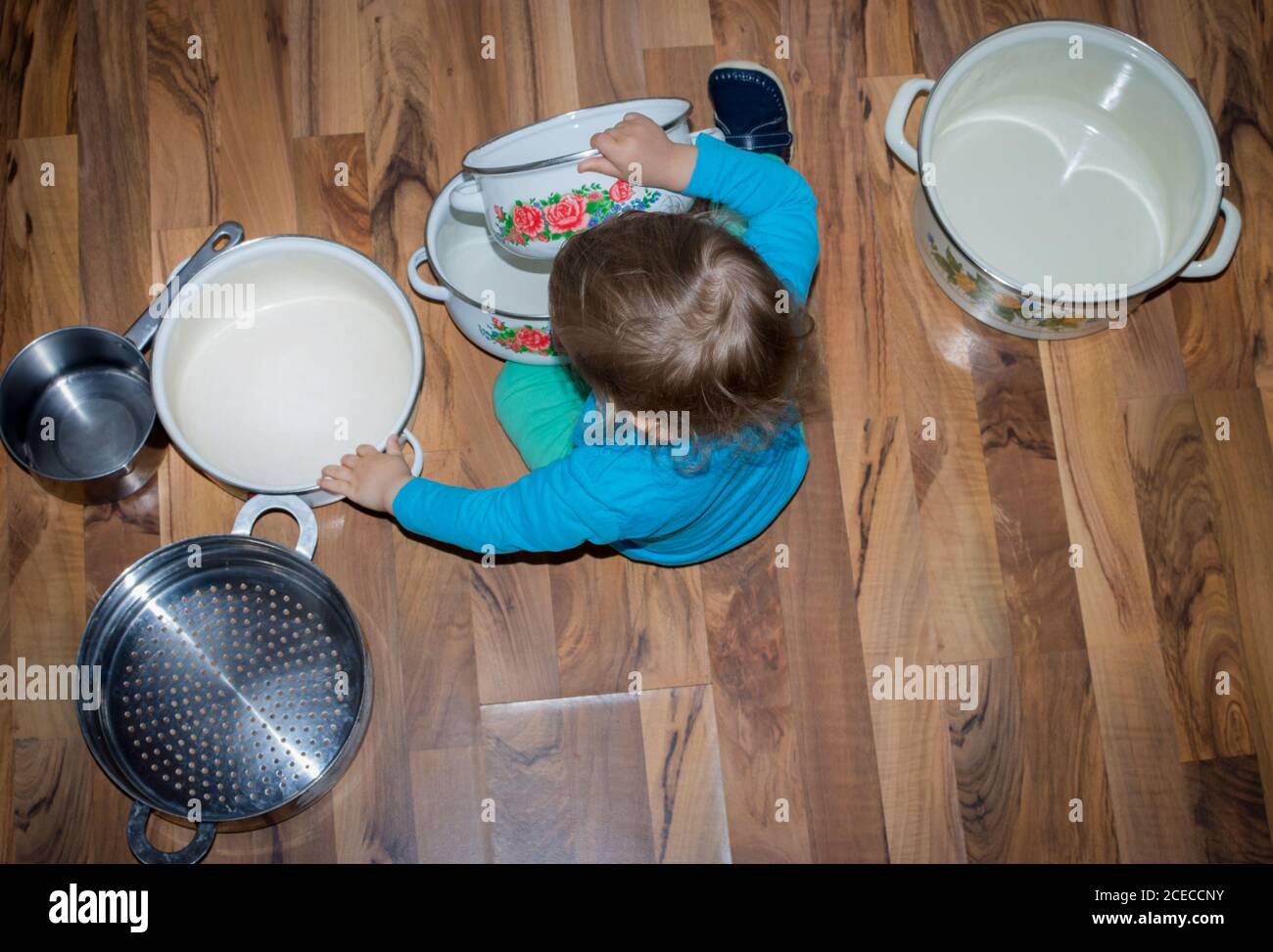 Cute little boy sitting on the kitchen floor playing with cooking pots ...