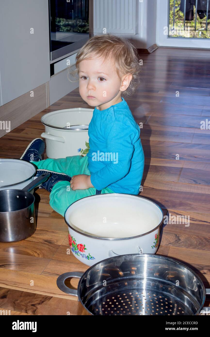Cute little boy sitting on the kitchen floor playing with cooking pots ...