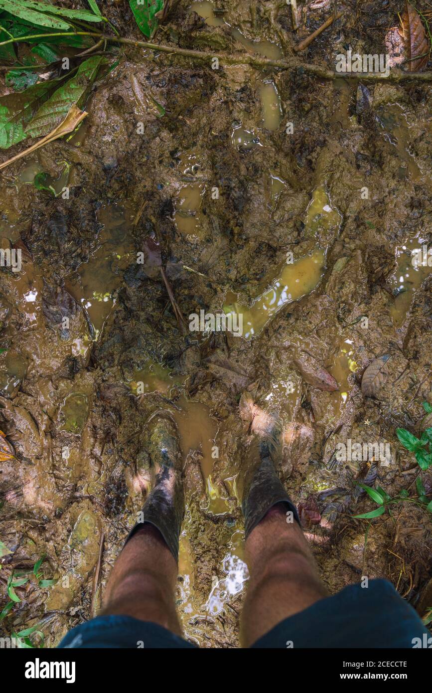 From above crop shot of man in gumboots standing in dirty mud with ...