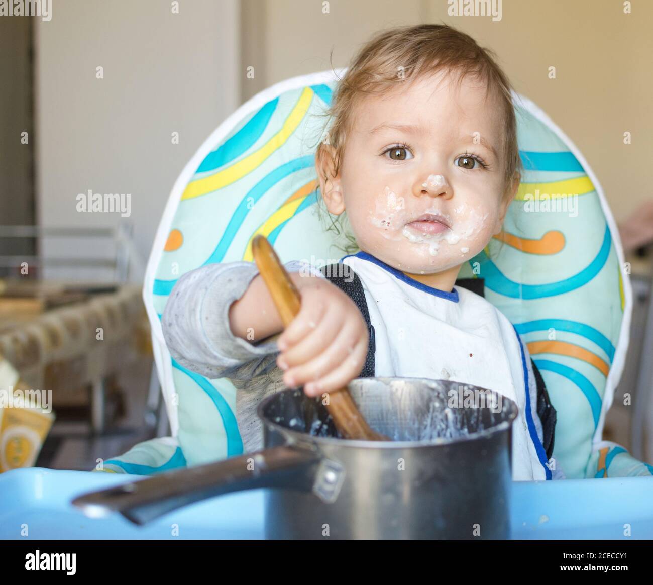 Funny baby child getting messy eating cereals or porridge by itself ...