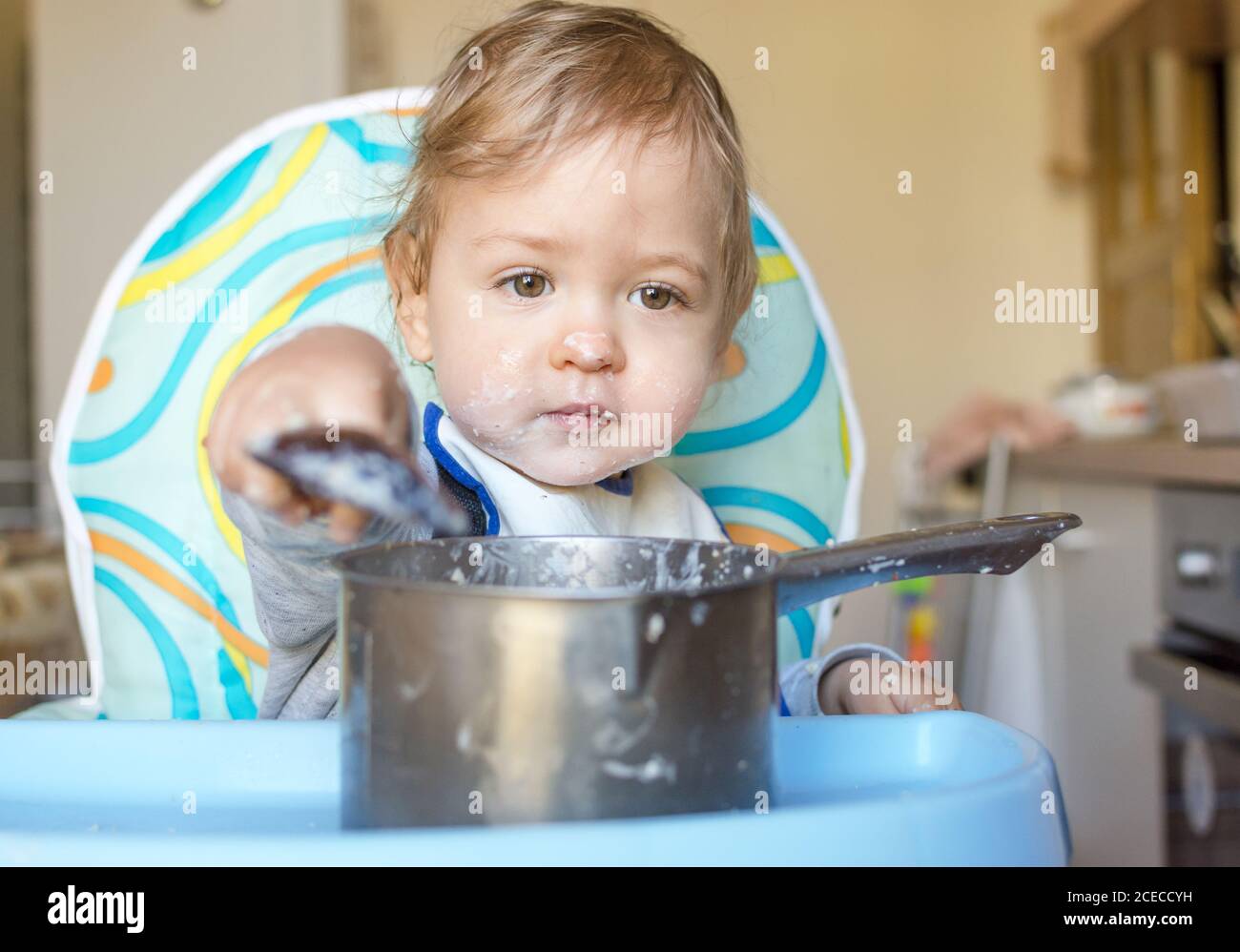 Funny baby child getting messy eating cereals or porridge by itself ...