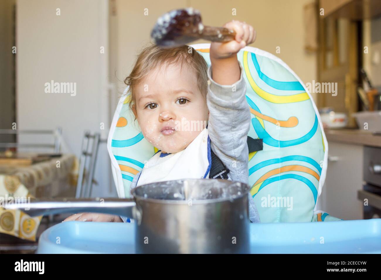 Funny baby child getting messy eating cereals or porridge by itself ...