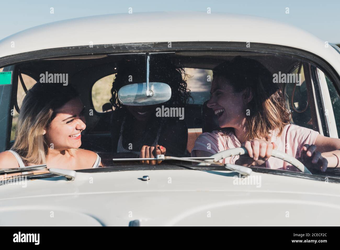 Group of happy multiethnic women in car driving together in bright ...