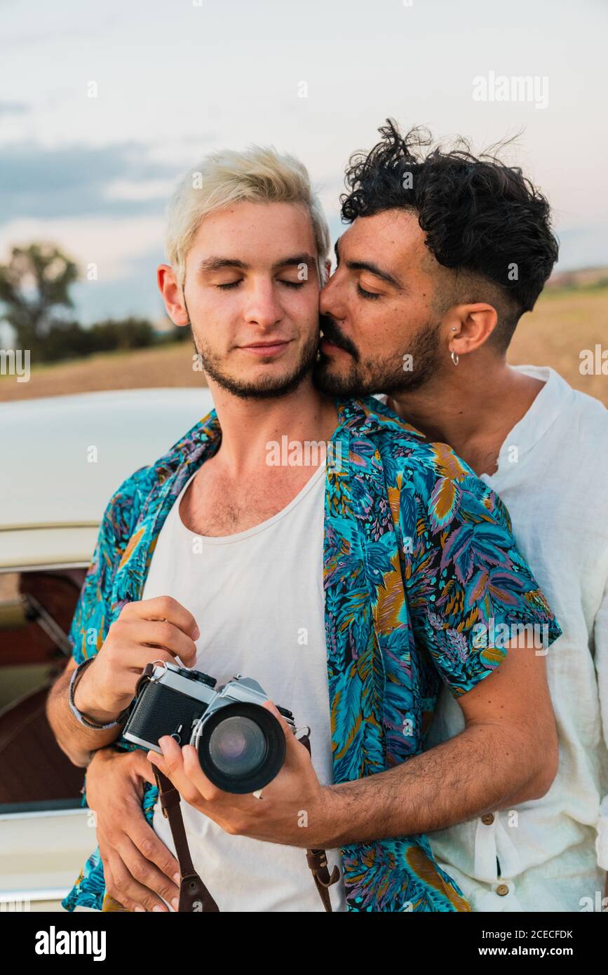 Kissing men in love embracing tenderly while standing with photo camera ...
