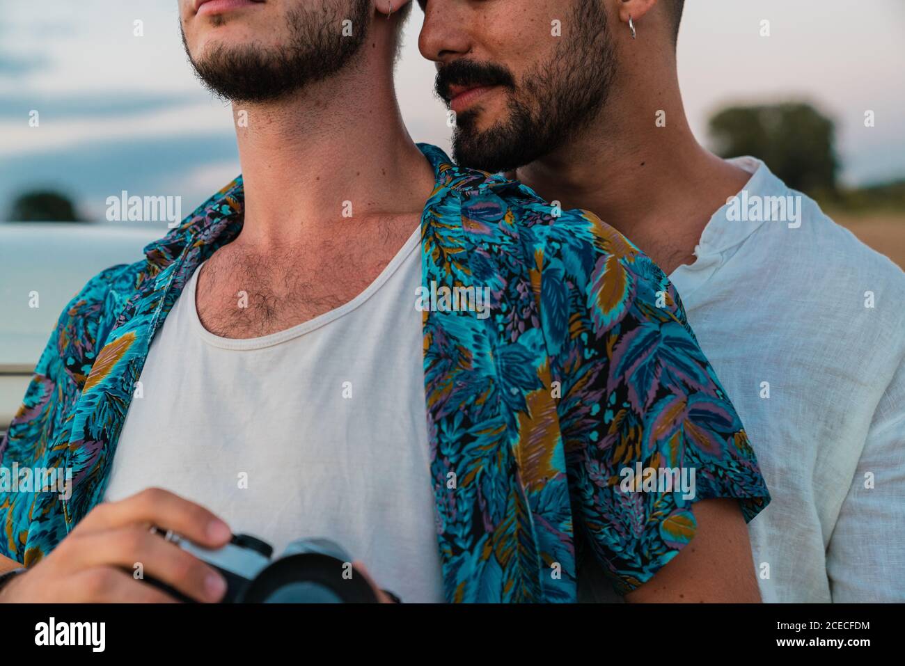 Kissing men in love embracing tenderly while standing with photo camera ...